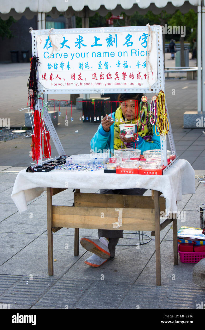 Street trader in Olympic Park, Beijing, China. The sign reads Carve ...