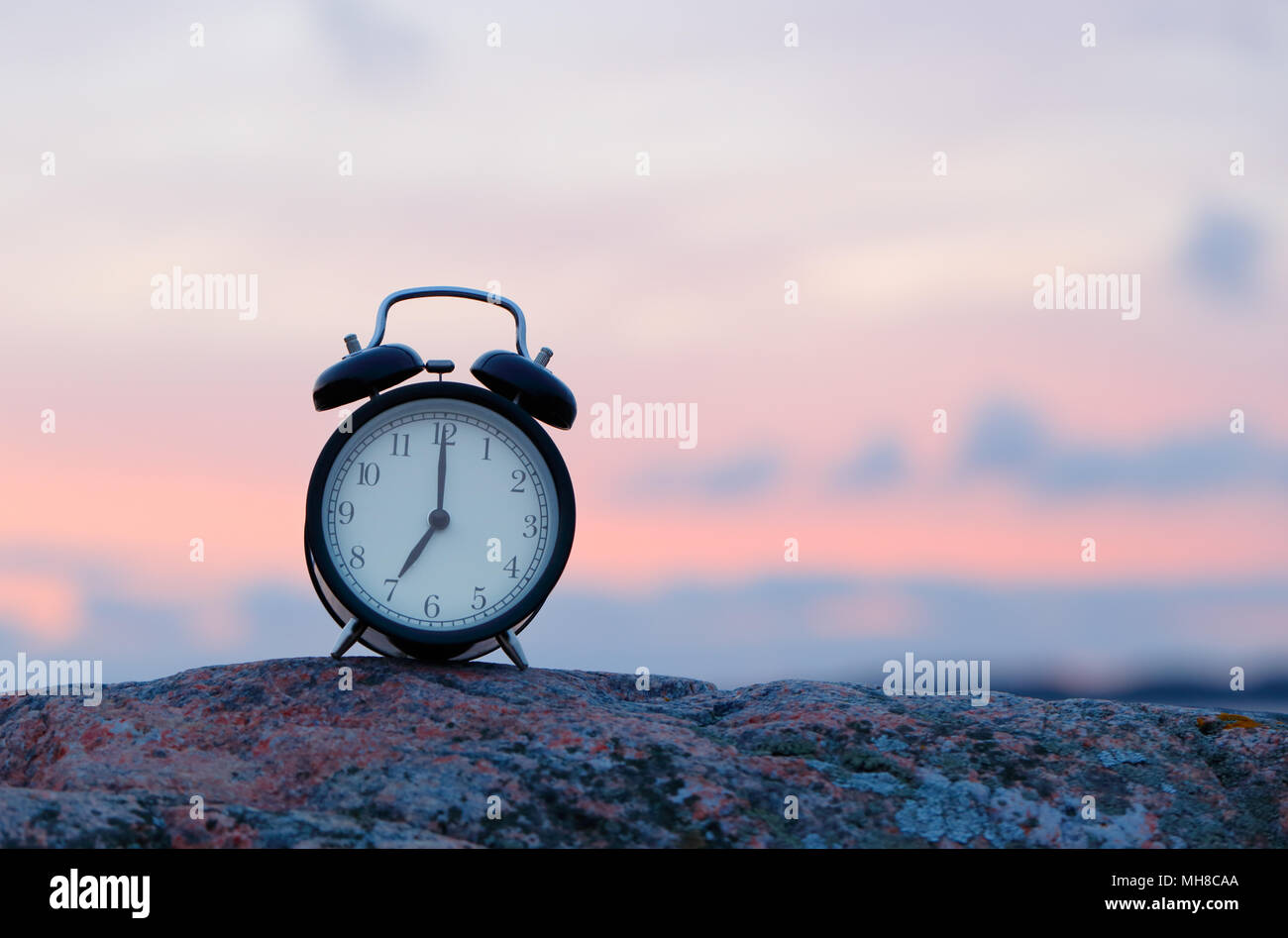 One black alarm clock on rock at seven o clock outdoor during sunrise ...