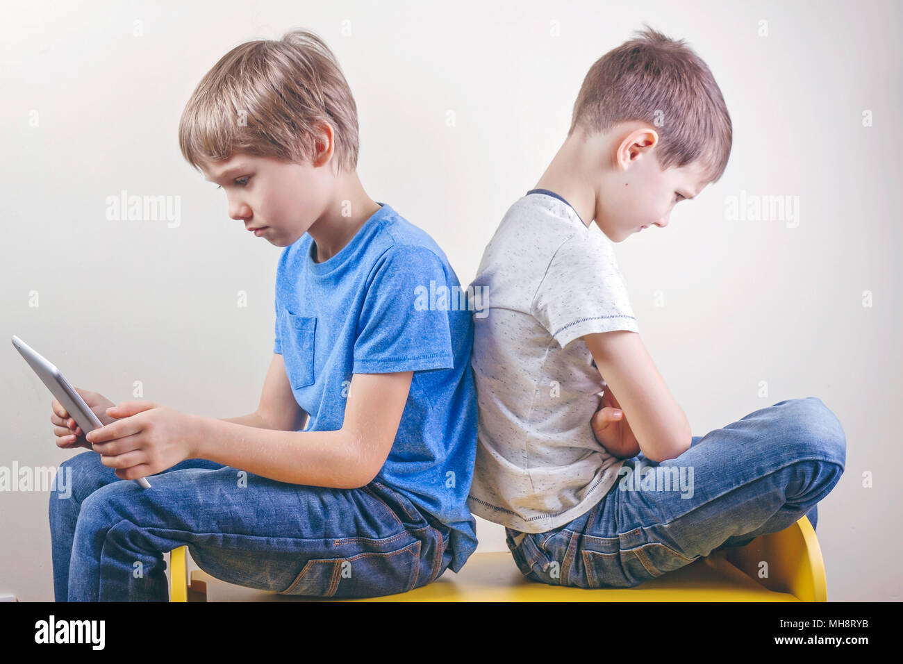 Computer addiction. One boy using tablet and other kid sitting angry ...