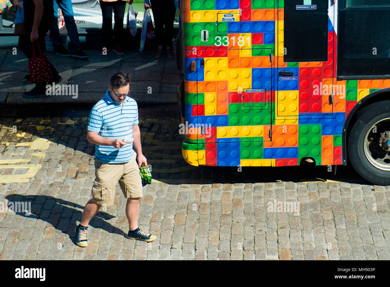 A pedestrian crossing the road in front of the rear end of a parked bus ...