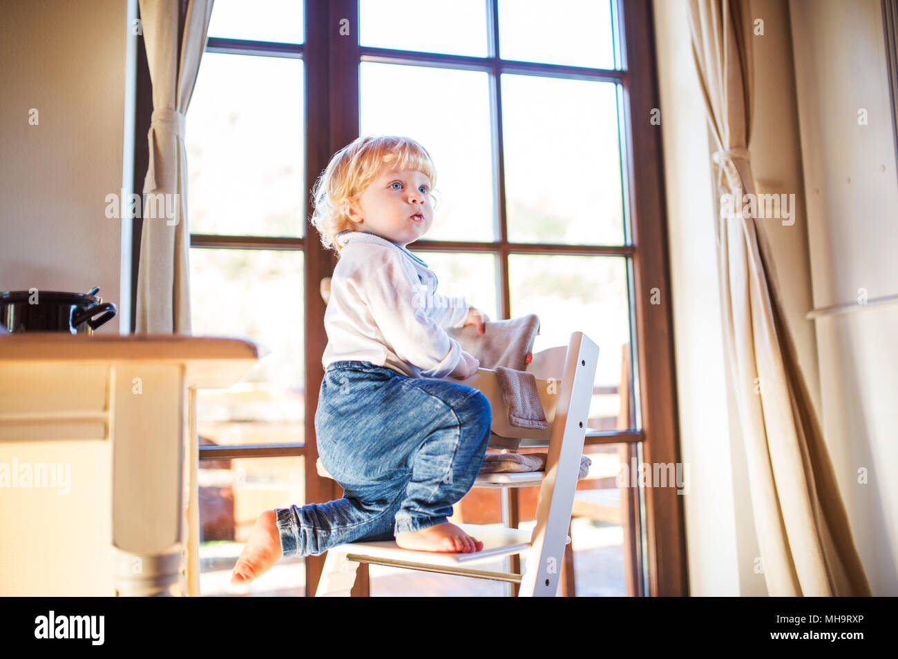 Toddler boy in a dangerous at home, climbing into highchair Stock Photo ...