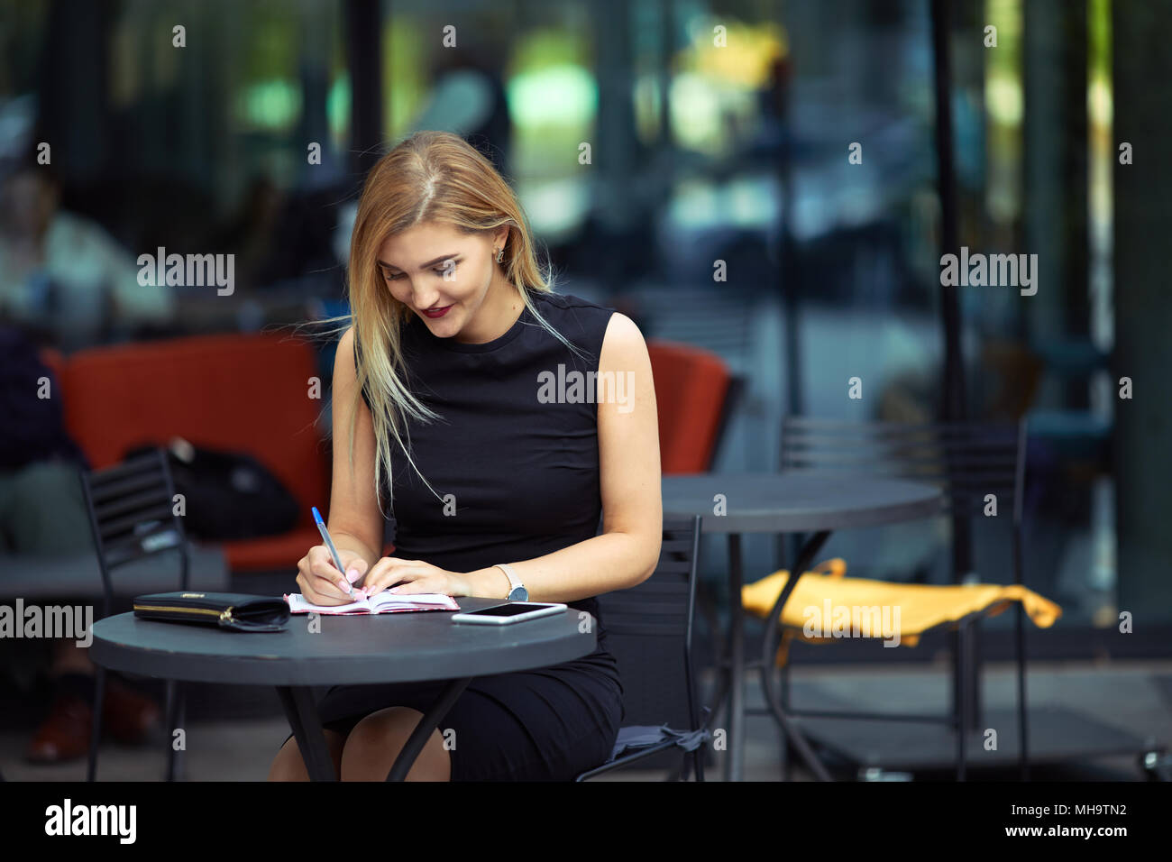 Beautiful girl sitting on the table and do her work, talk at phone ...