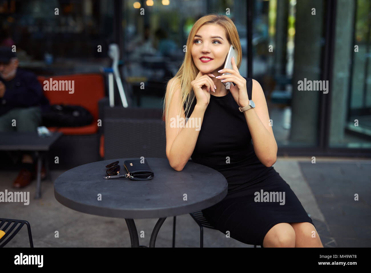 Beautiful girl sitting on the table and do her work, talk at phone ...