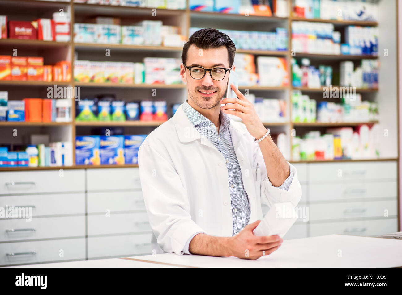 Young friendly male pharmacist with smartphone, making a phone call ...