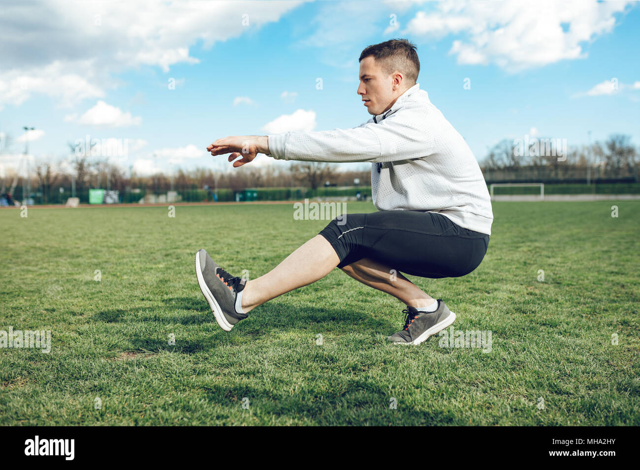 Active young man stretching and doing one leg crouching exercises in ...