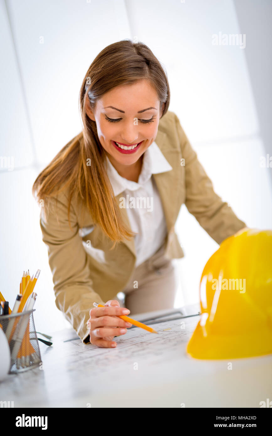Smiling young woman architect constructor analyzing blueprint at desk ...