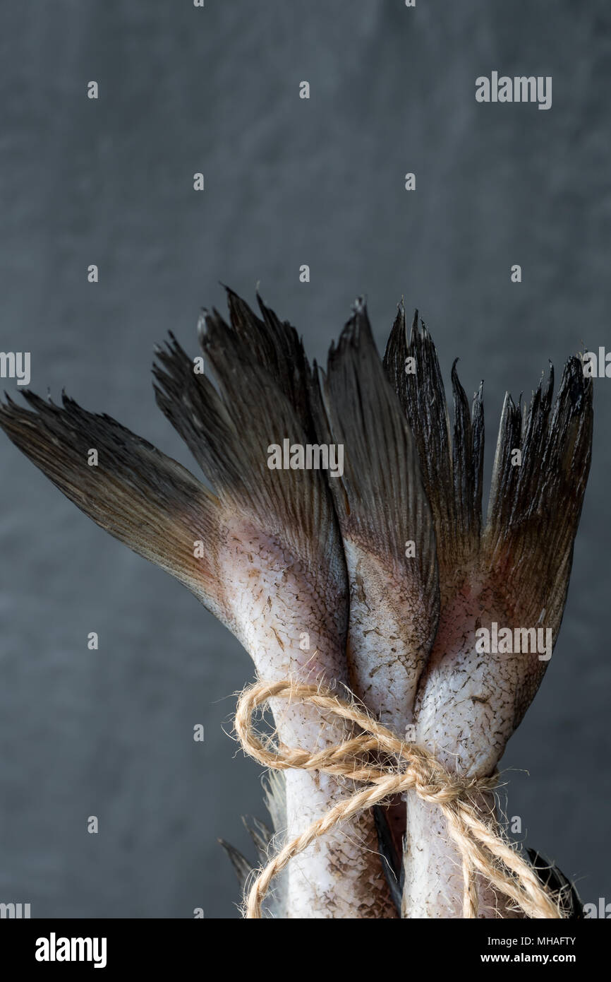 Raw fish tails tied with rope with bow on dark background. Selective ...