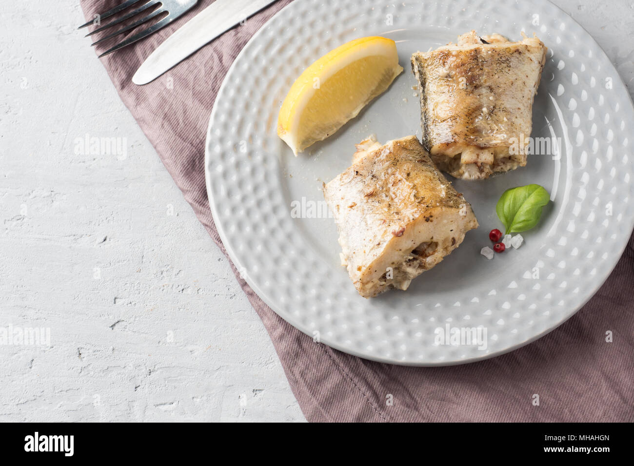Baked Pollock fish with lemon and spices on a plate Napkin on the table ...