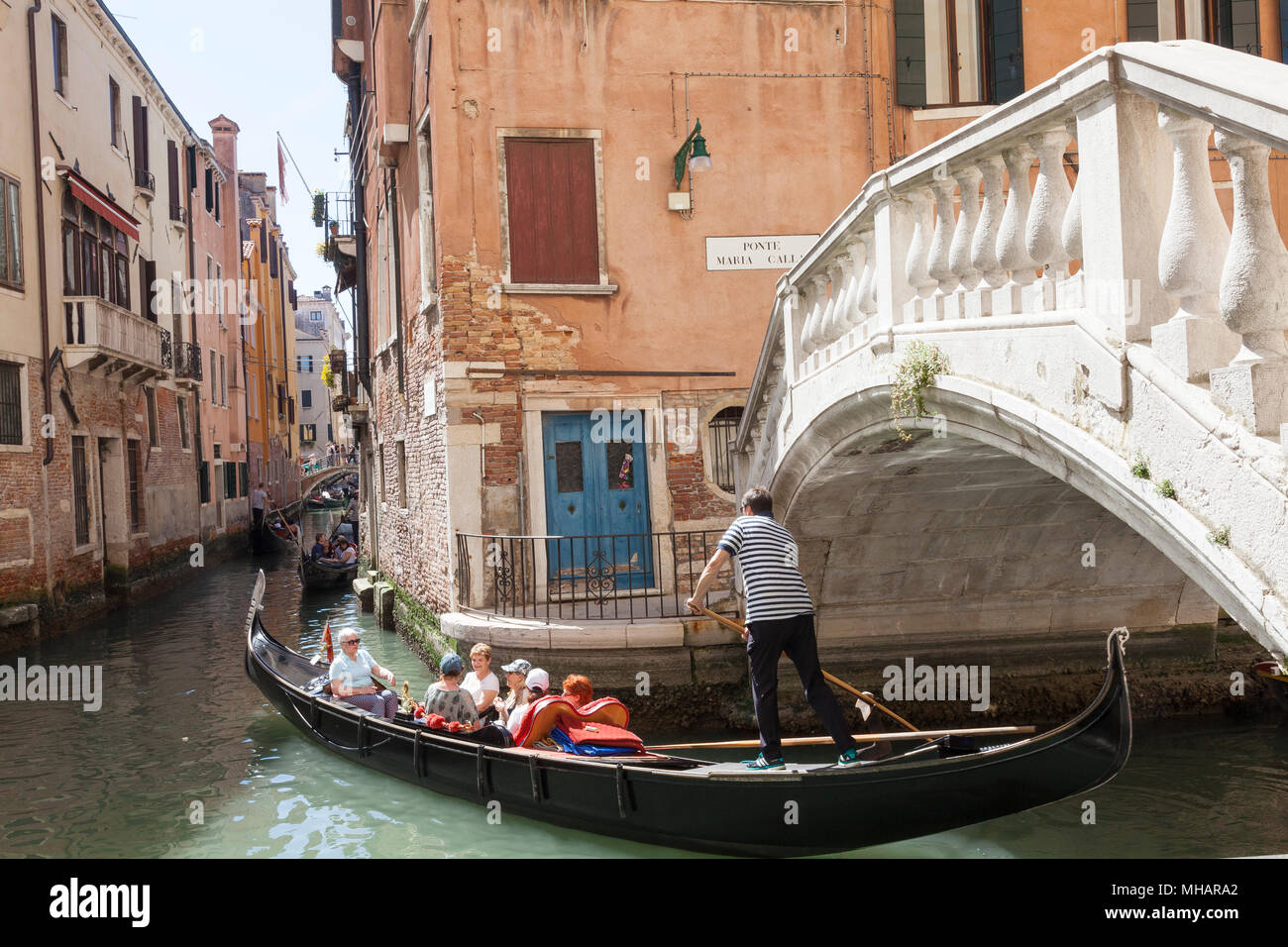 Gondolier navigating a busy narrow back canal in his gondola with ...