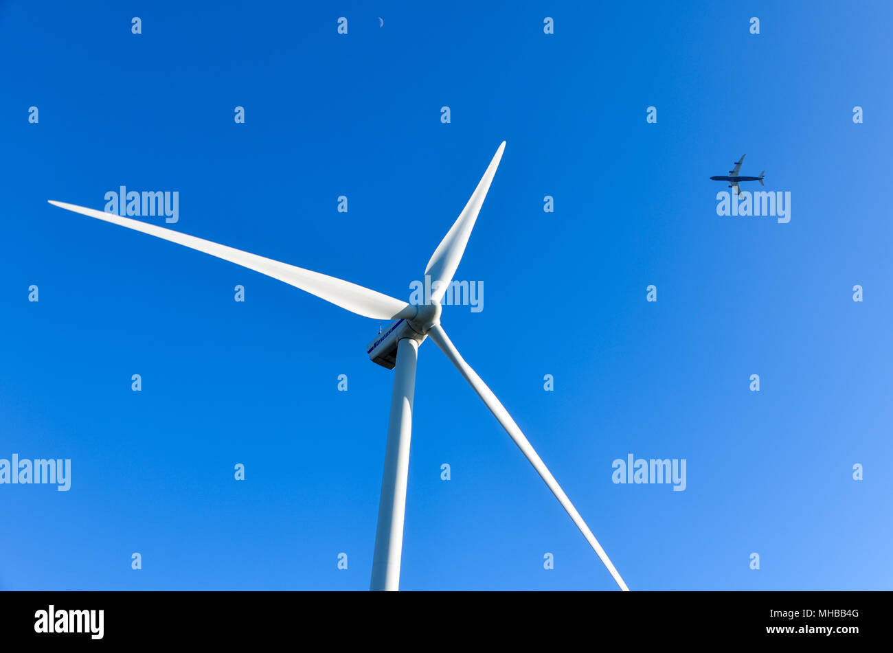 Plane flying behind a wind turbine on a blue sky background Stock Photo ...