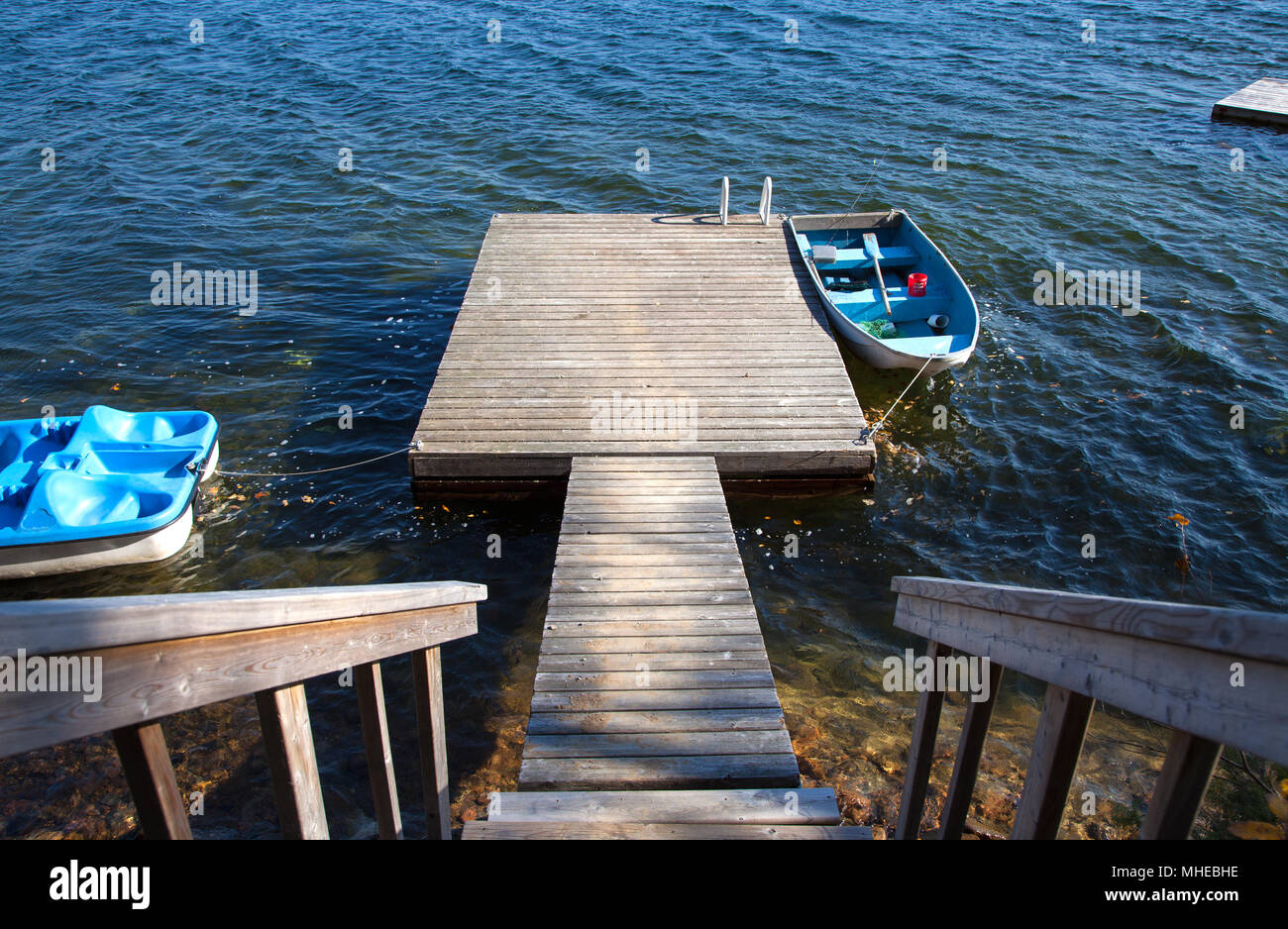 Paddle boat and fishing boat tied to a wooden lakeside dock with ...