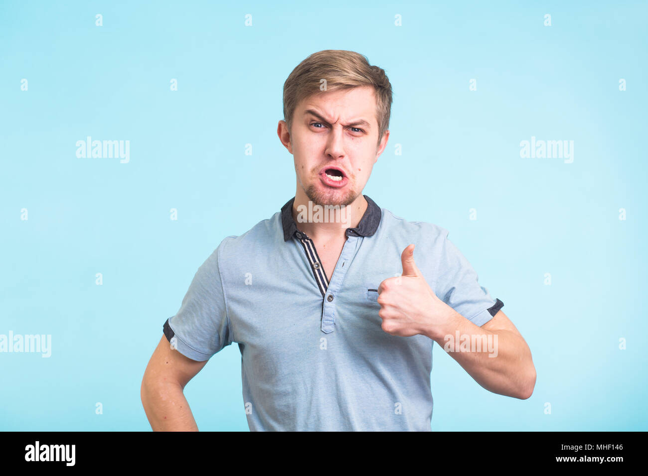 Funny angry man showing thumbs up on blue background Stock Photo - Alamy