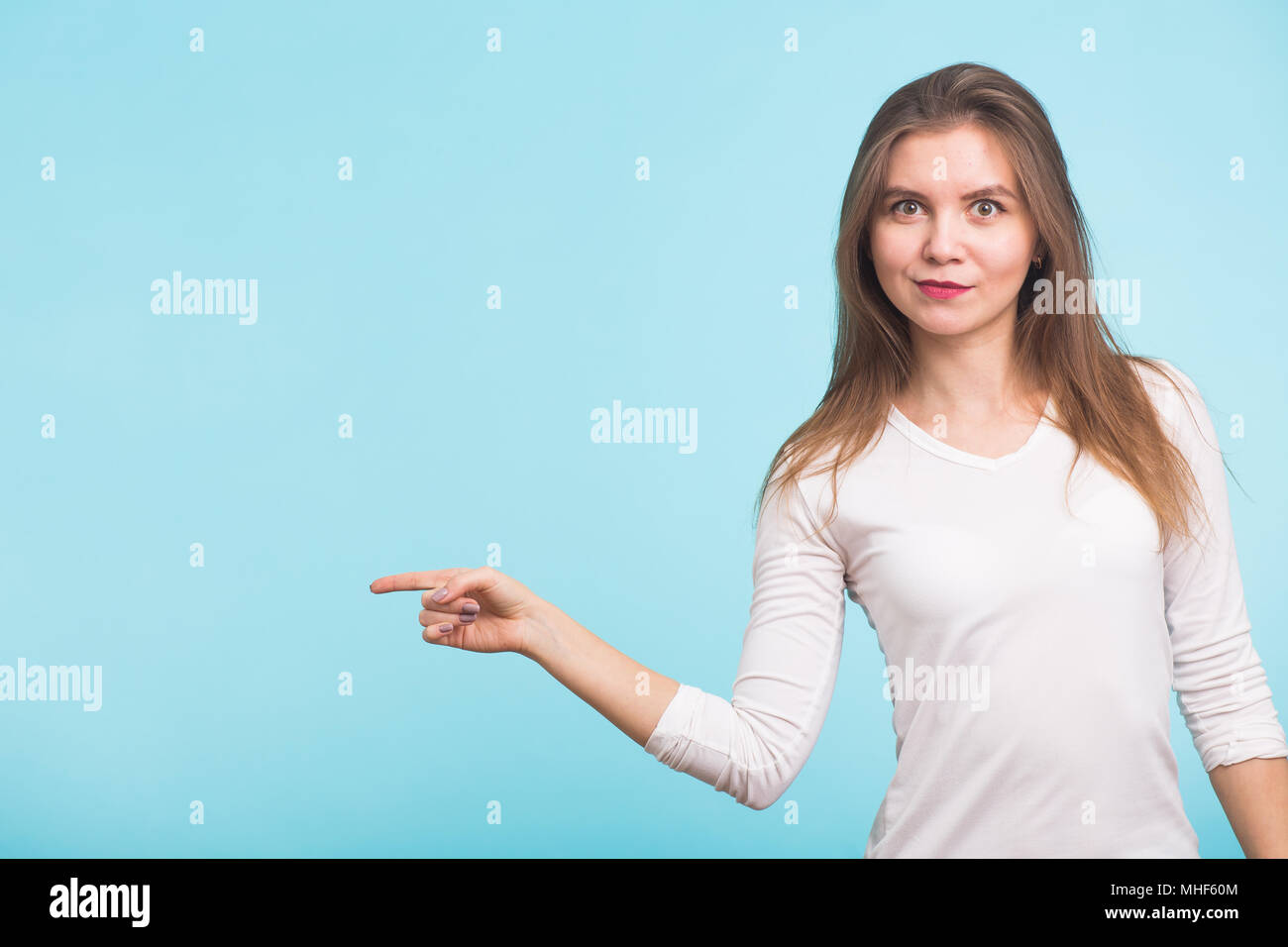 Young woman pointing at copy space on blue background Stock Photo - Alamy