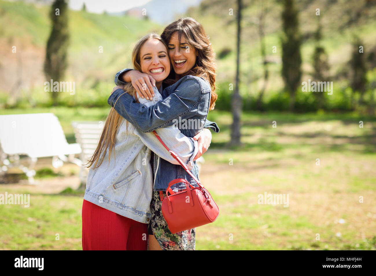 Two happy girls hugging in urban park. Blonde and brunette girls ...