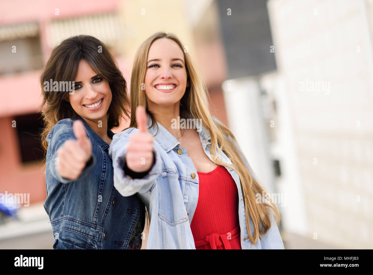 Two funny women friends with thumbs up and looking at the camera in ...