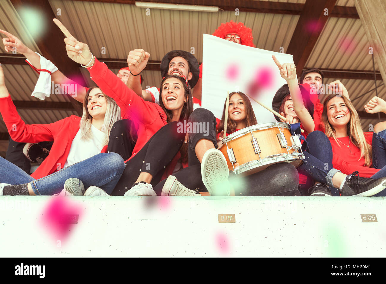 young group of fans dressed in red color watching a sports event in the ...