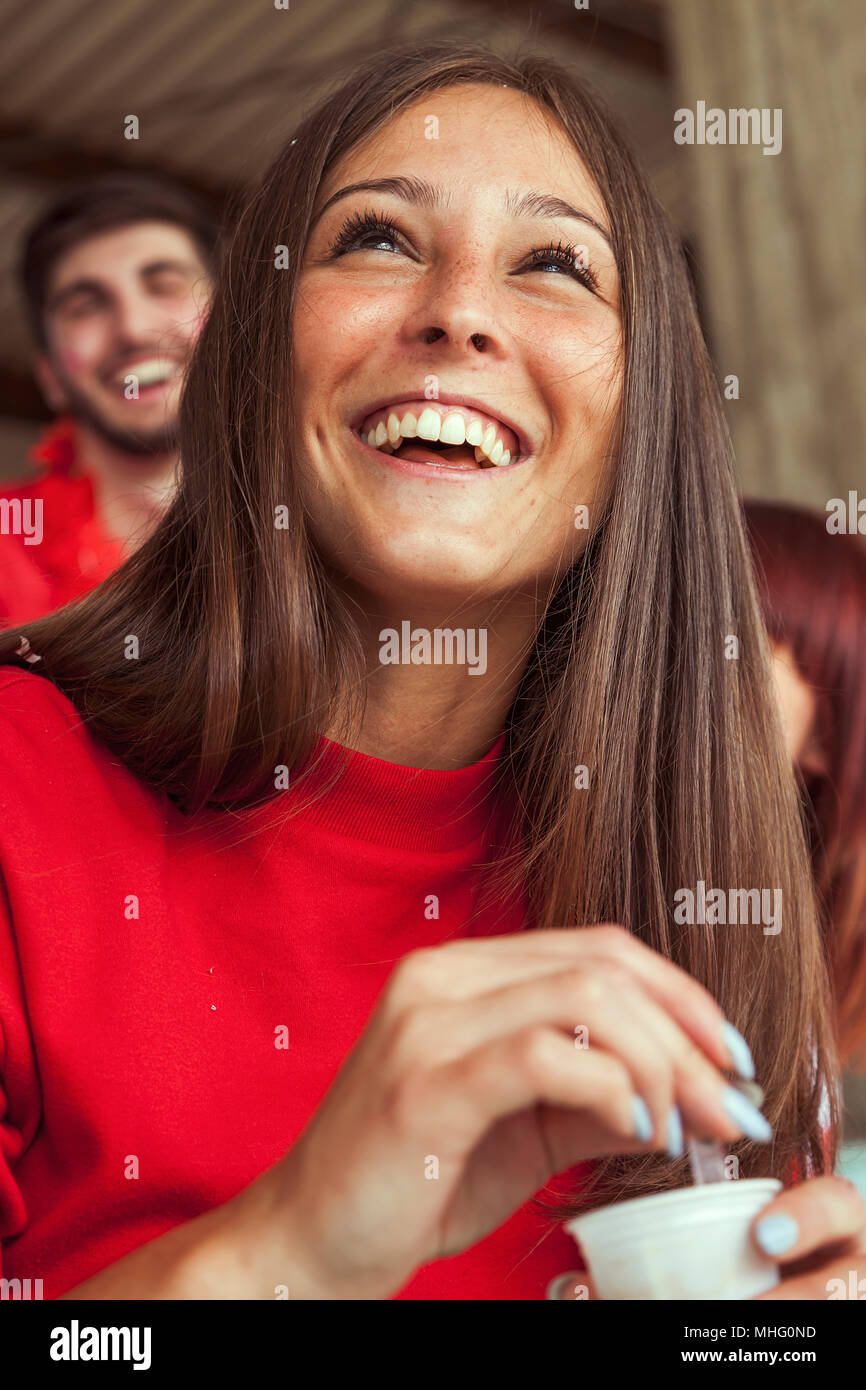 young female supporter fan dressed in red color relaxing drinking a cup ...