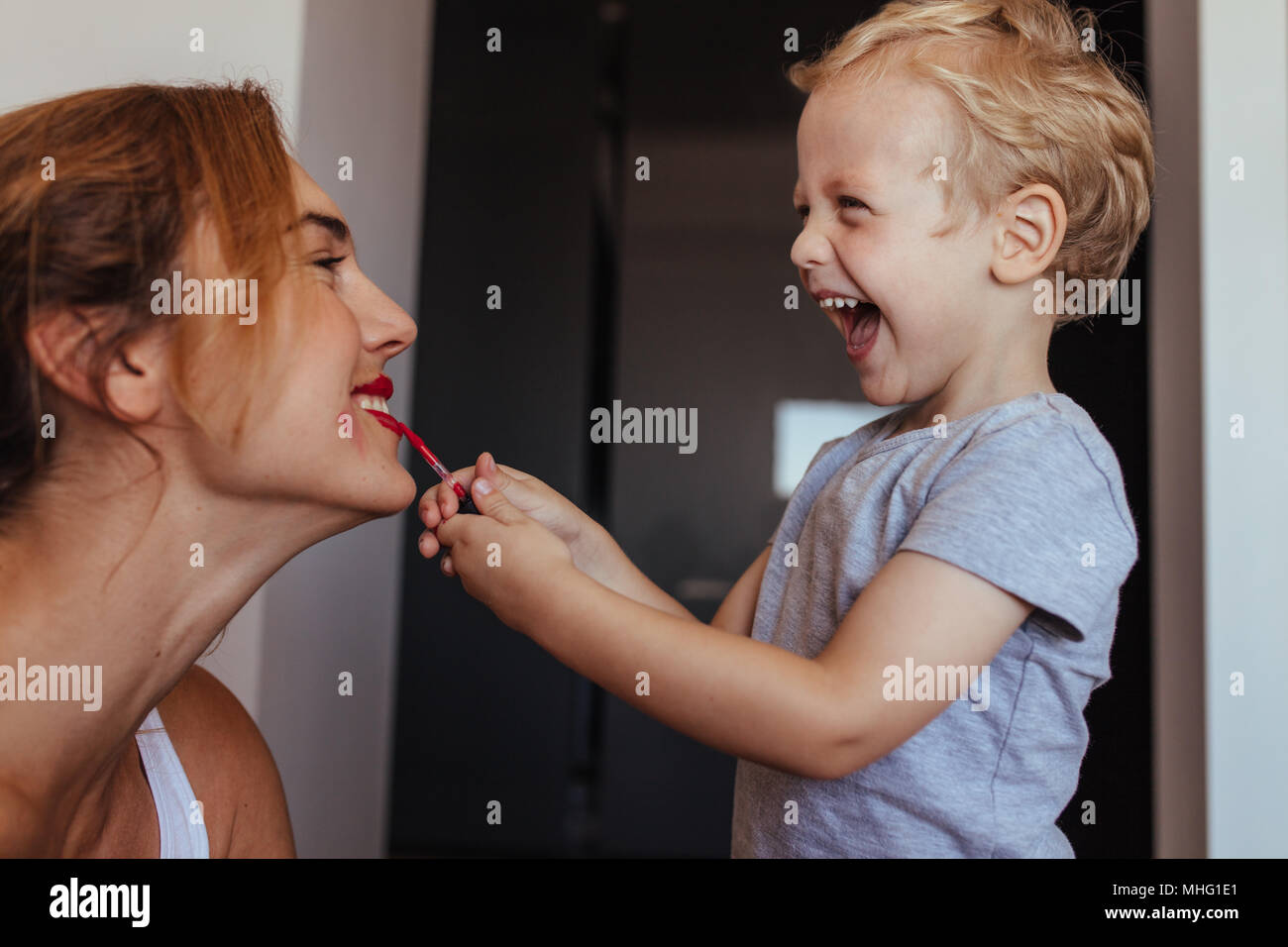 Smiling little boy putting on the makeup to her mother. Happy mother ...