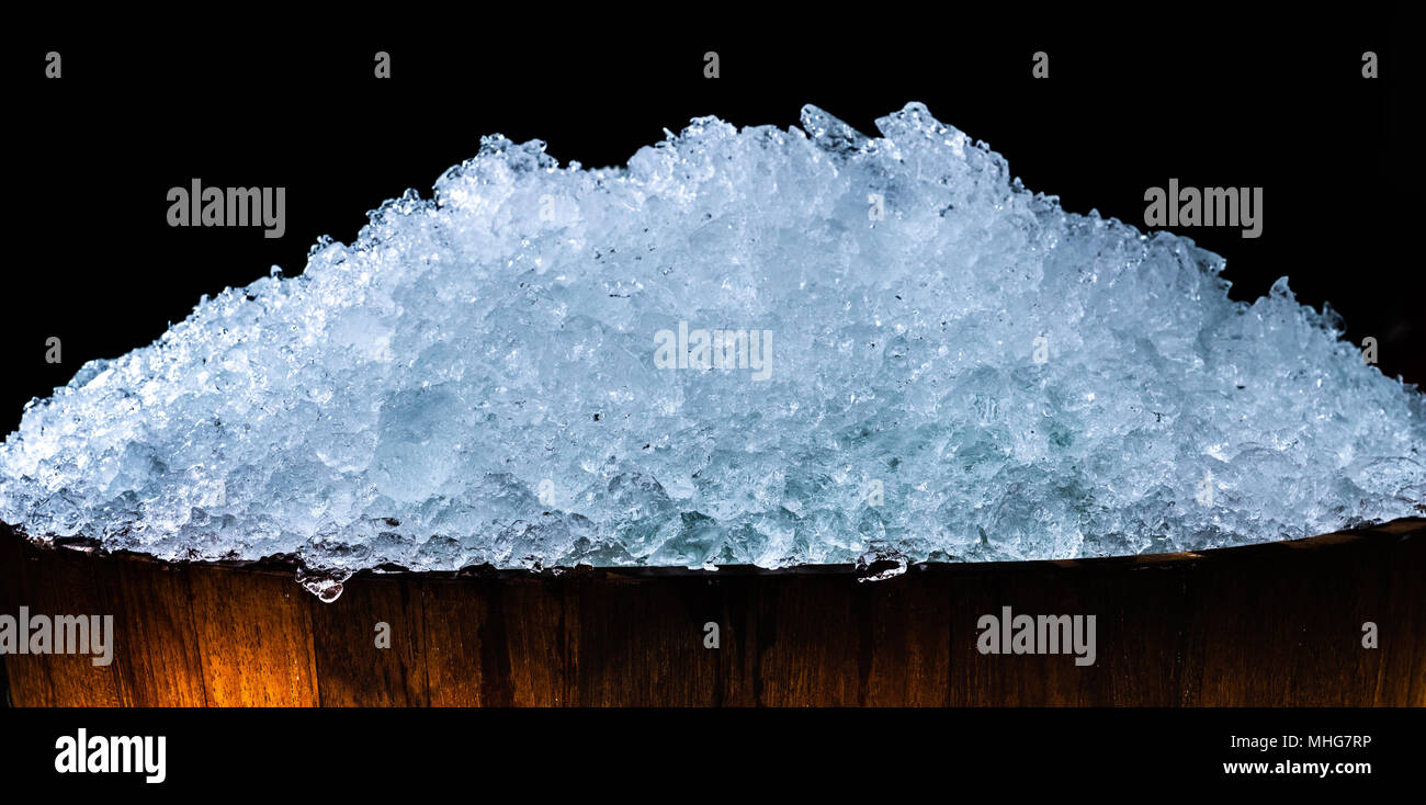 Pile of crushed ice cubes in wood bucket on dark background with copy ...