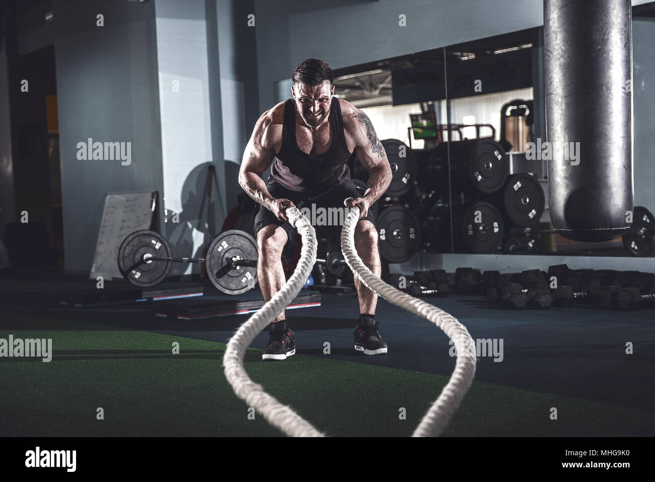 Muscular powerful aggressive man working out with rope in functional ...