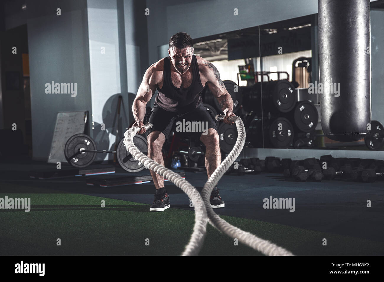 Muscular powerful aggressive man working out with rope in functional ...