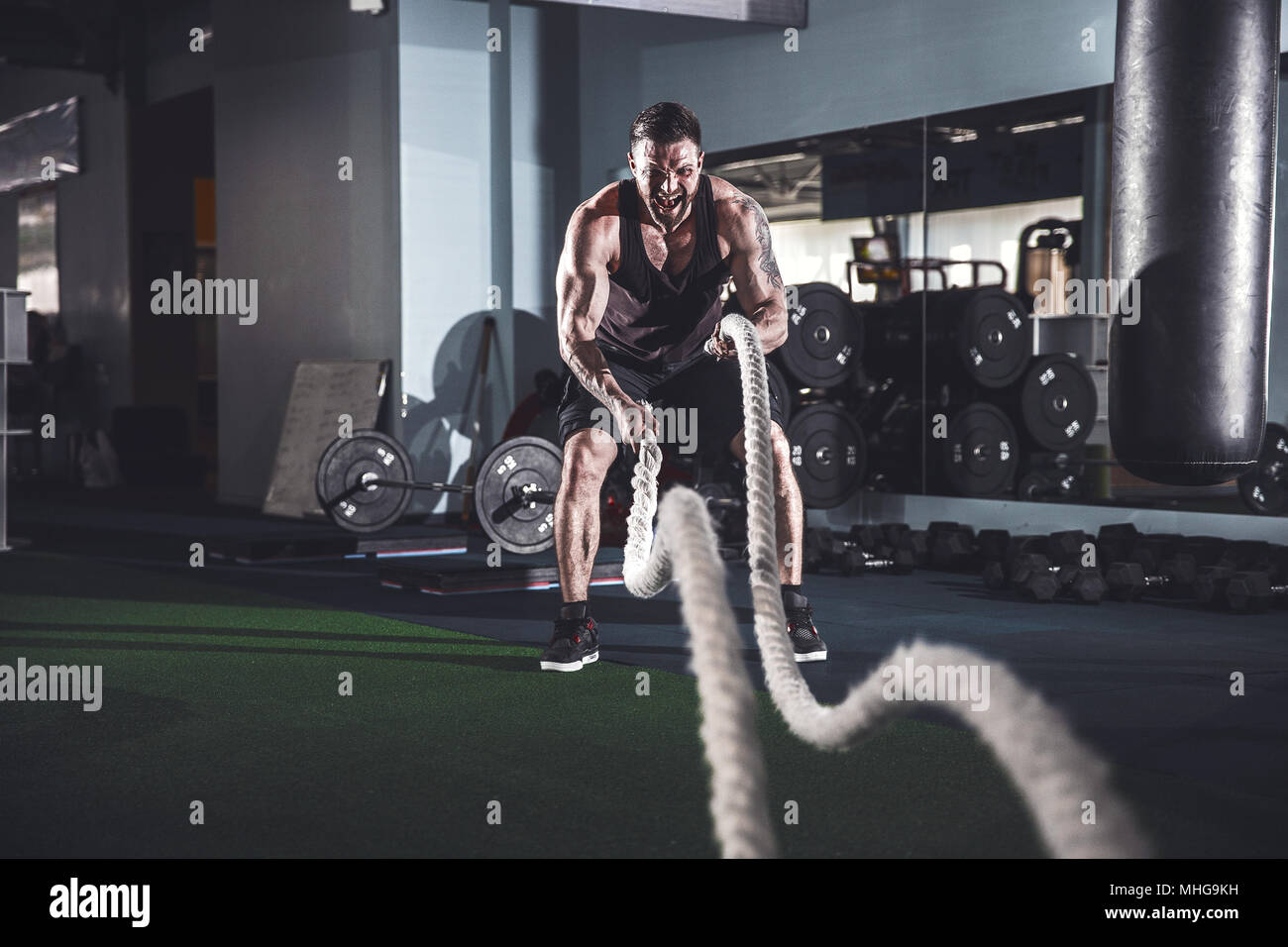 Muscular powerful aggressive man working out with rope in functional ...