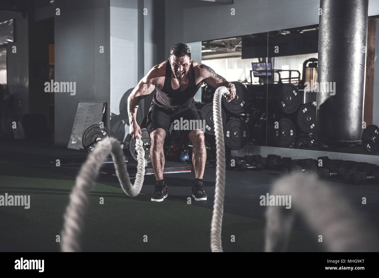 Muscular powerful aggressive man working out with rope in functional ...