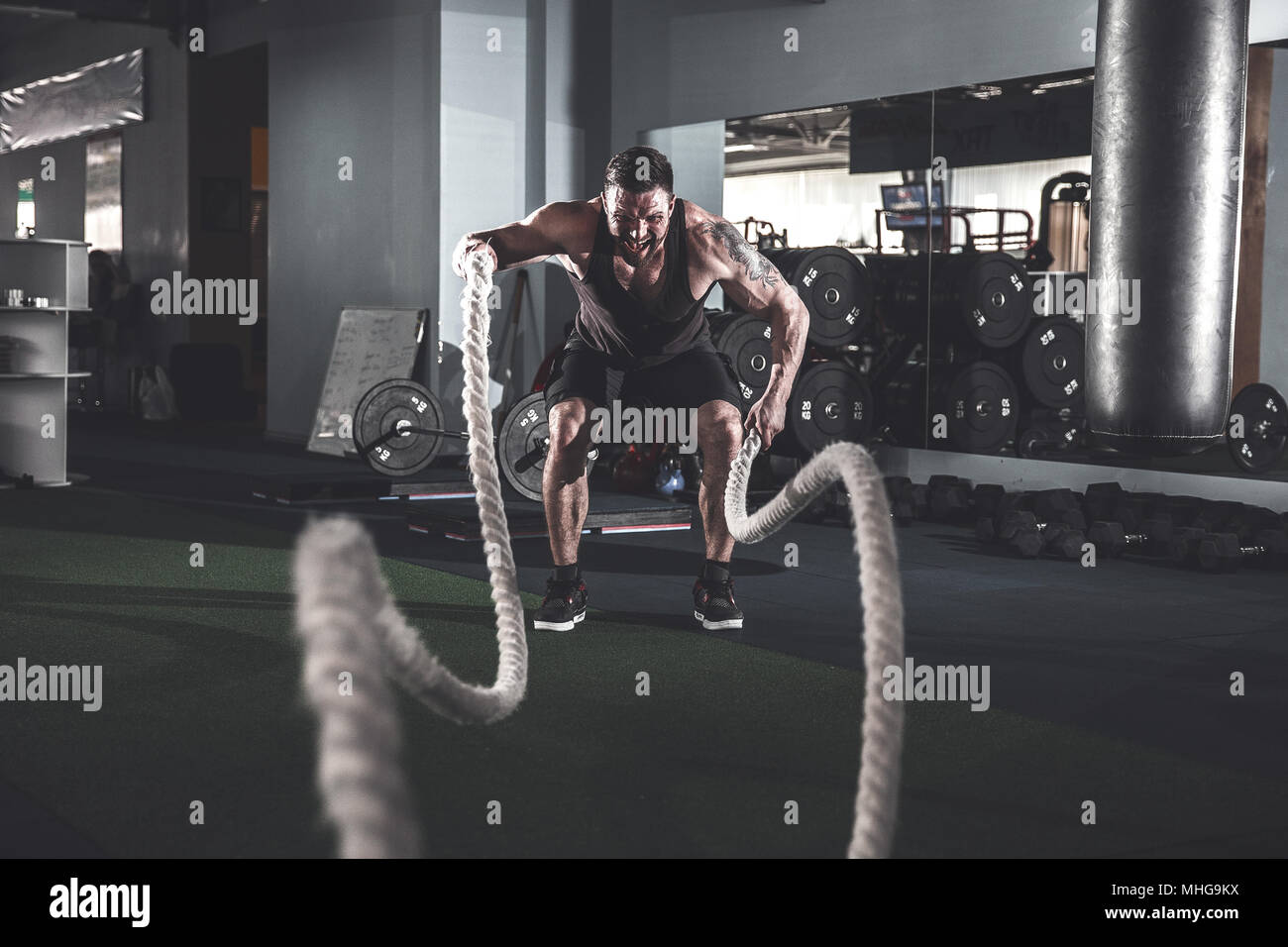Muscular powerful aggressive man working out with rope in functional ...
