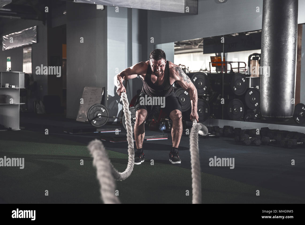Muscular powerful aggressive man working out with rope in functional ...