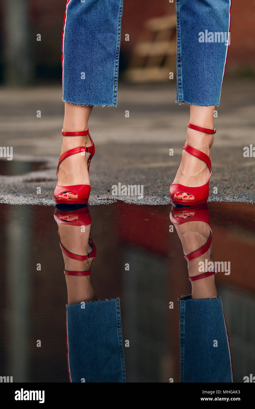 Reflection of female legs in jeans and red shoes in puddle on asphalt ...