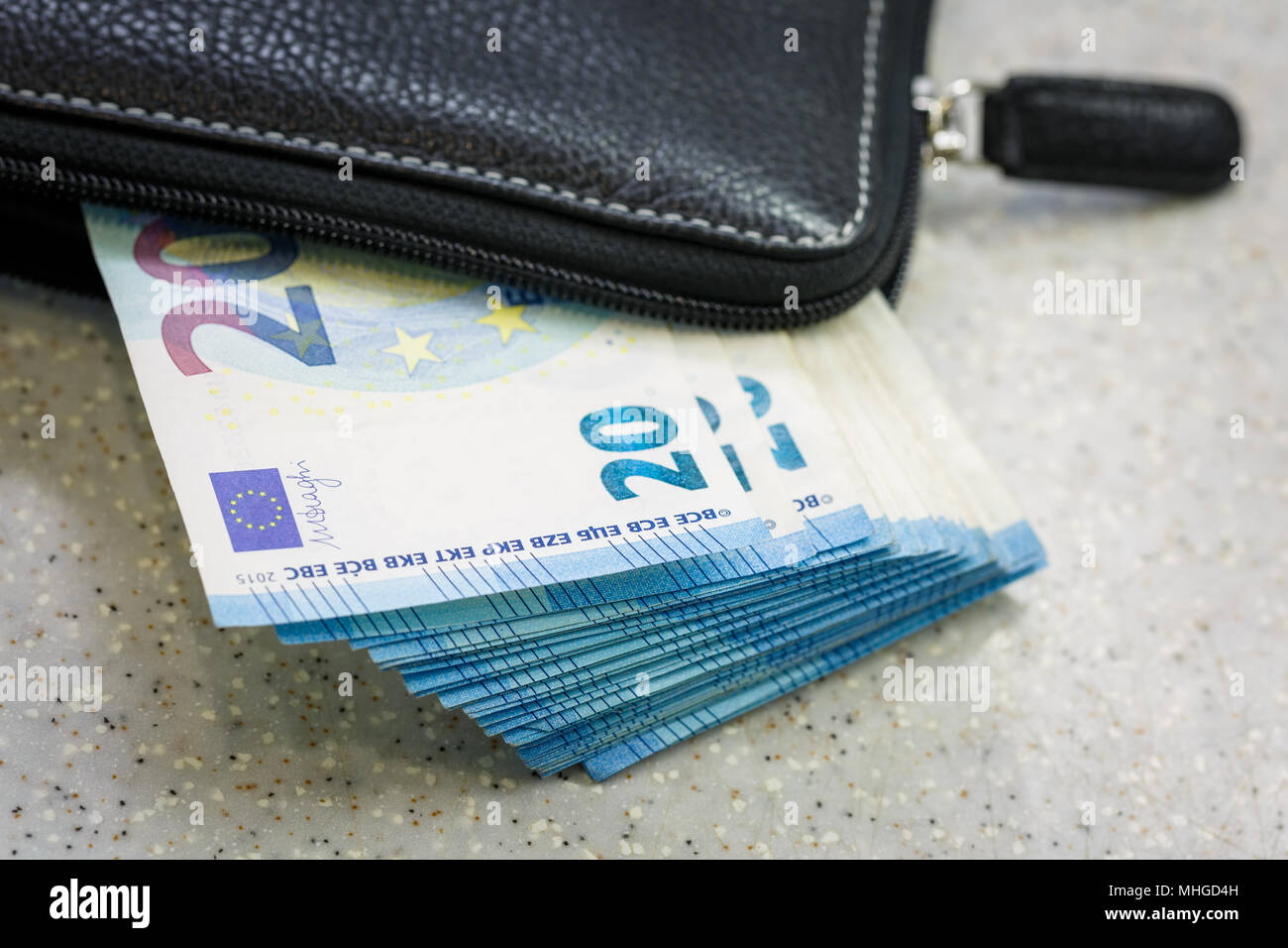 Black leather purse and wad of cash 20 euros are lie on the grey table ...