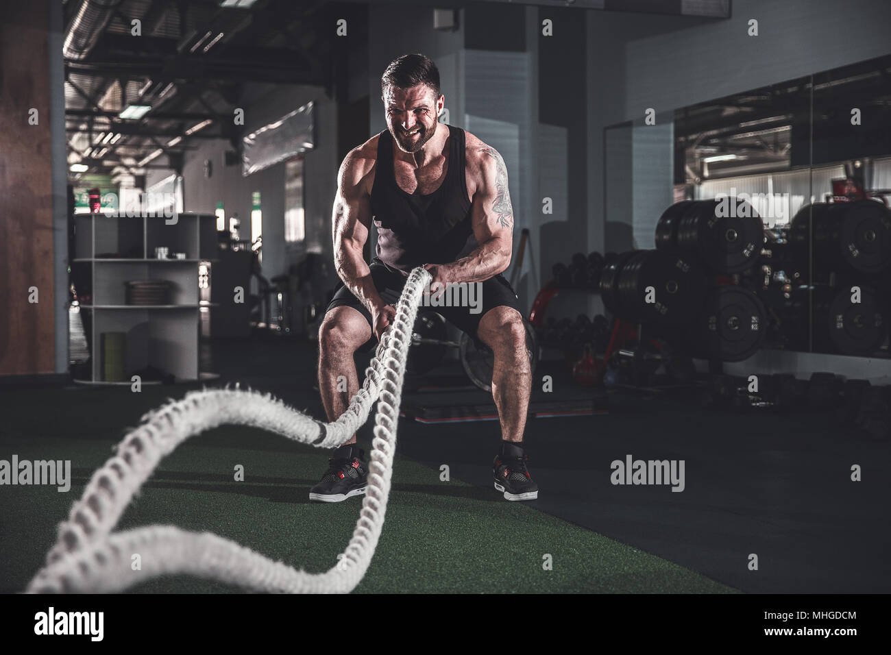 Muscular powerful aggressive man working out with rope in functional ...