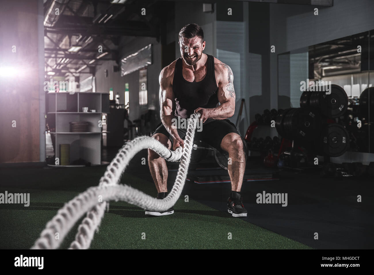 Muscular powerful aggressive man working out with rope in functional ...