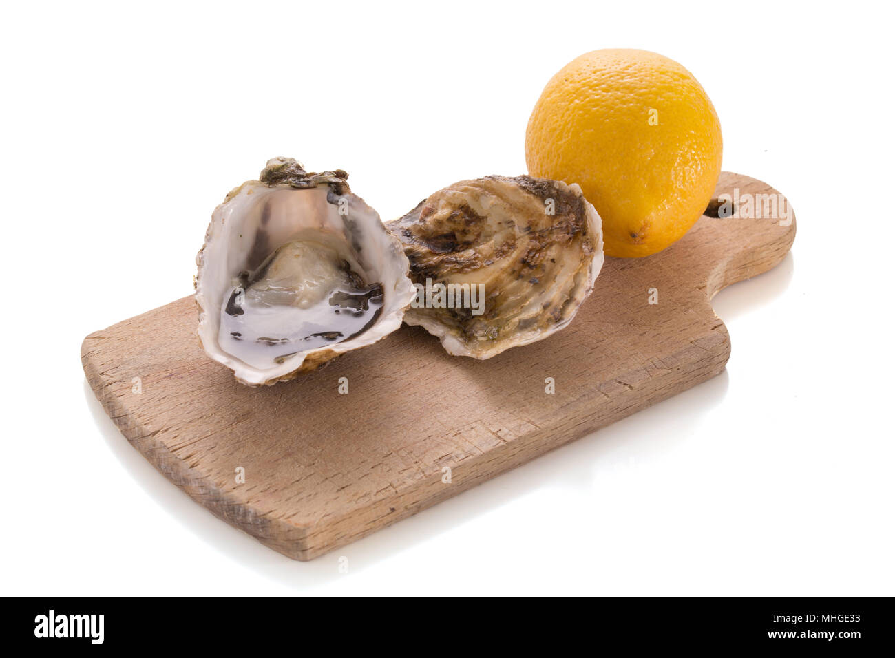An open oyster and a closed oyster on a wooden cutting board on a white ...