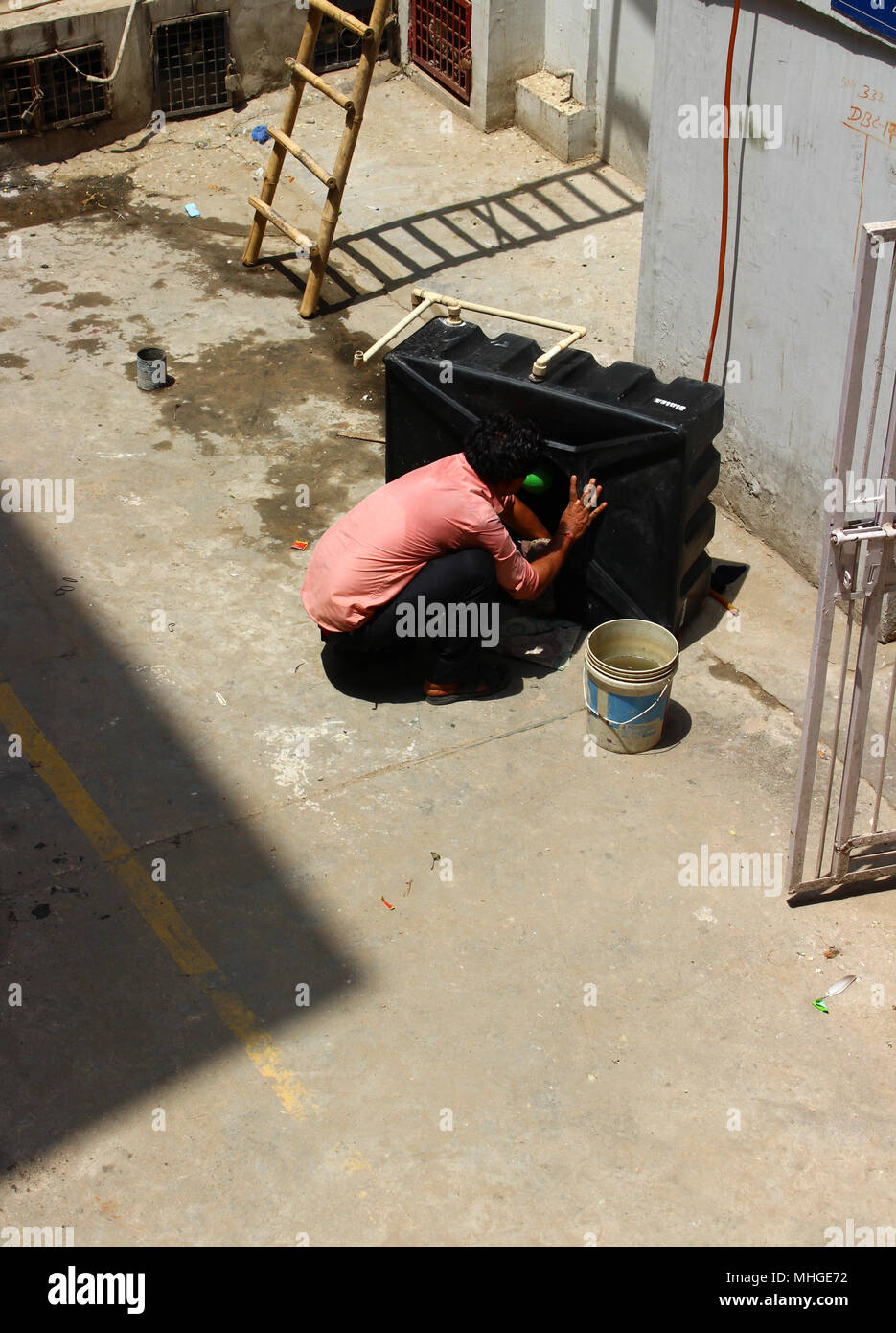 Man cleaning an overhead water tank lying on ground in Delhi, India ...
