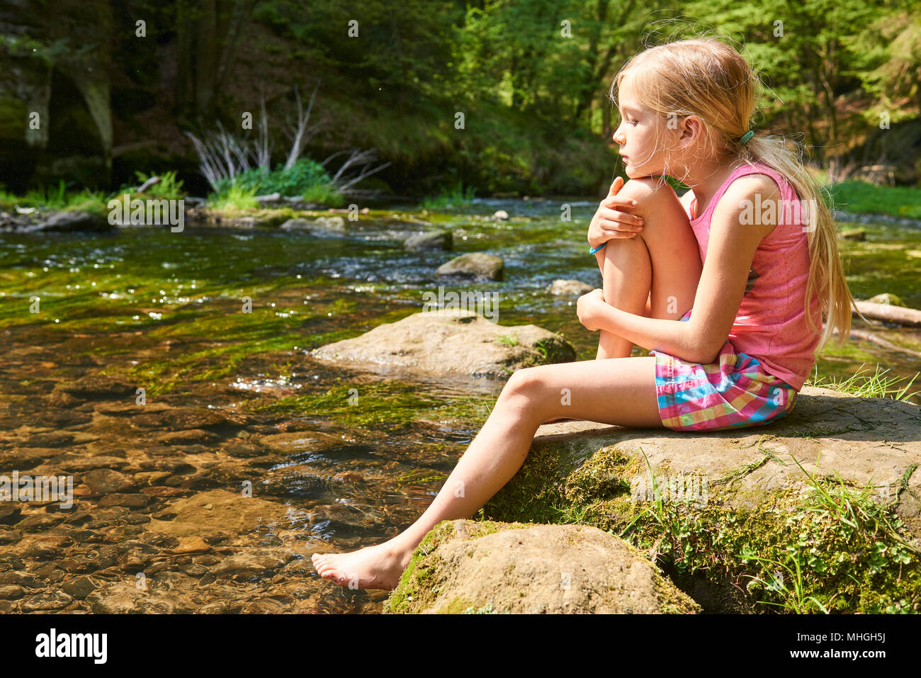 Child blond girl sitting on a rock by the river summer sunlight Stock ...