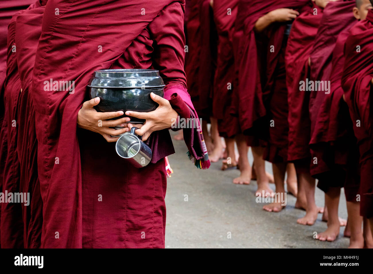 Detail of buddhist monks crowd in red robes and person holding a bowl ...