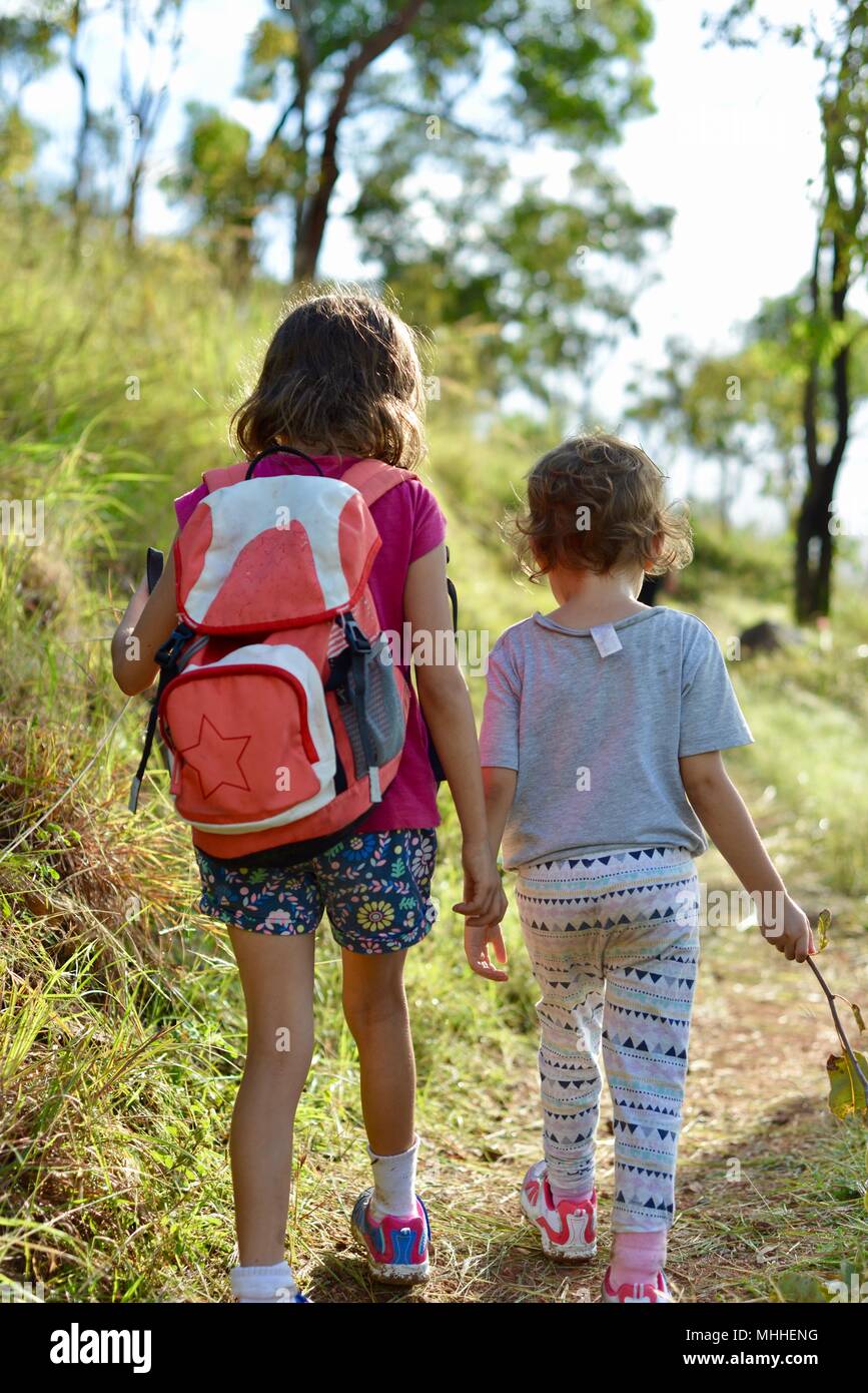 Two children walking on a gravel path in a forest with natural lighting ...