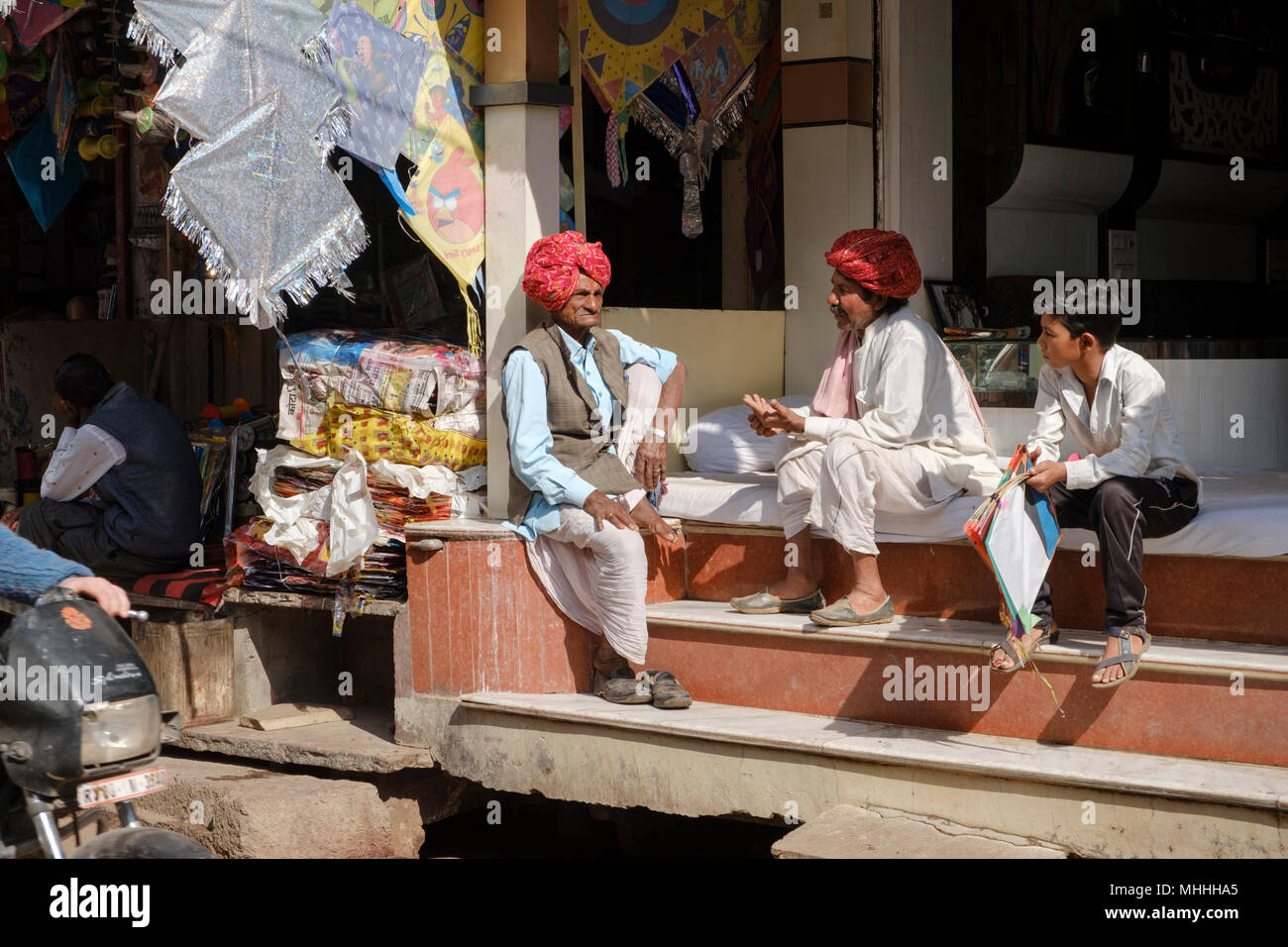 Two men in traditional red turbans and a young boy sit outside their ...