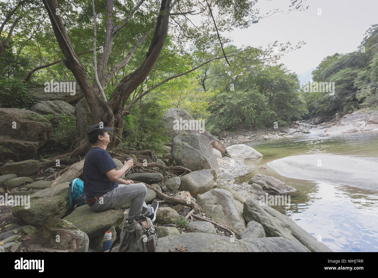 A man sitting beside a stream enjoying the scenery Stock Photo - Alamy
