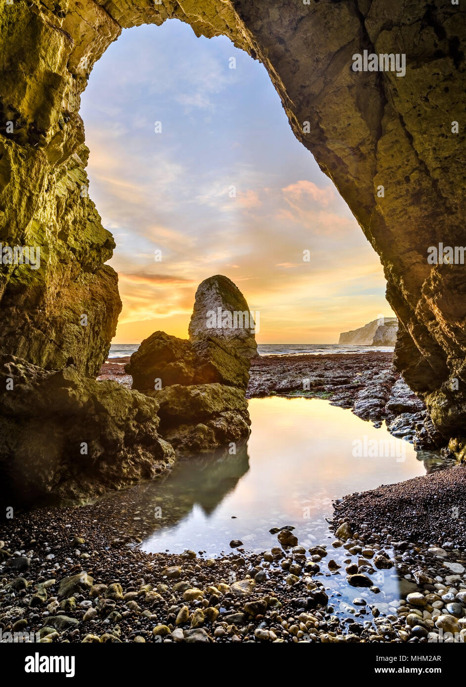 View of rocks through a cave and rockpools at sunset on the coast ...