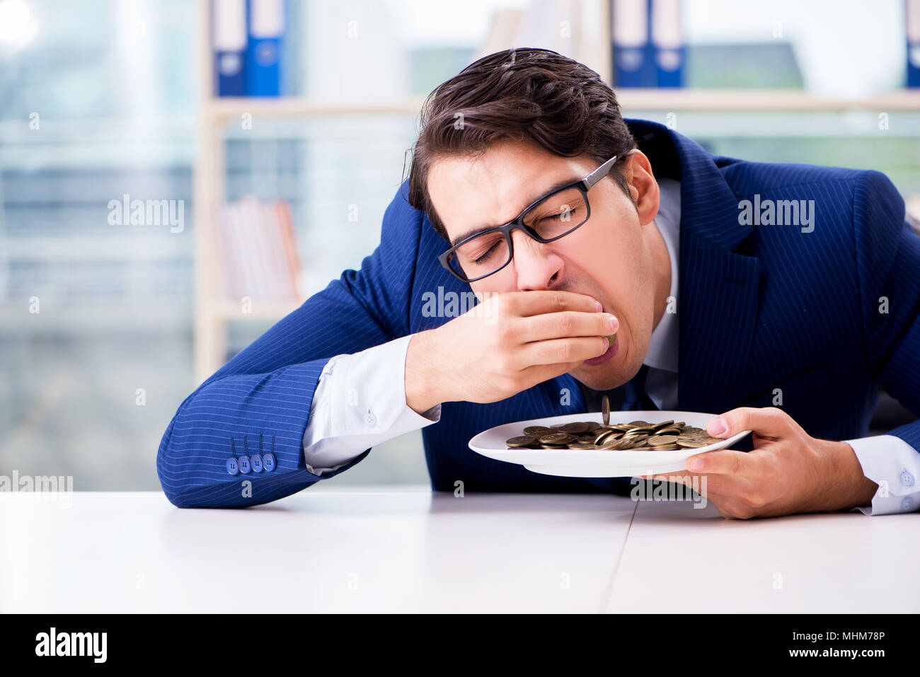 Funny businessman eating gold coins in office Stock Photo - Alamy