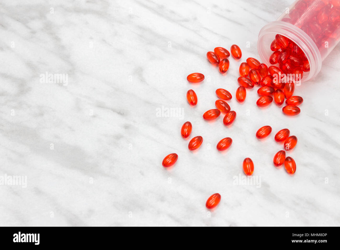 Bottle with red shiny pills on marble background. Capsules spilling out ...