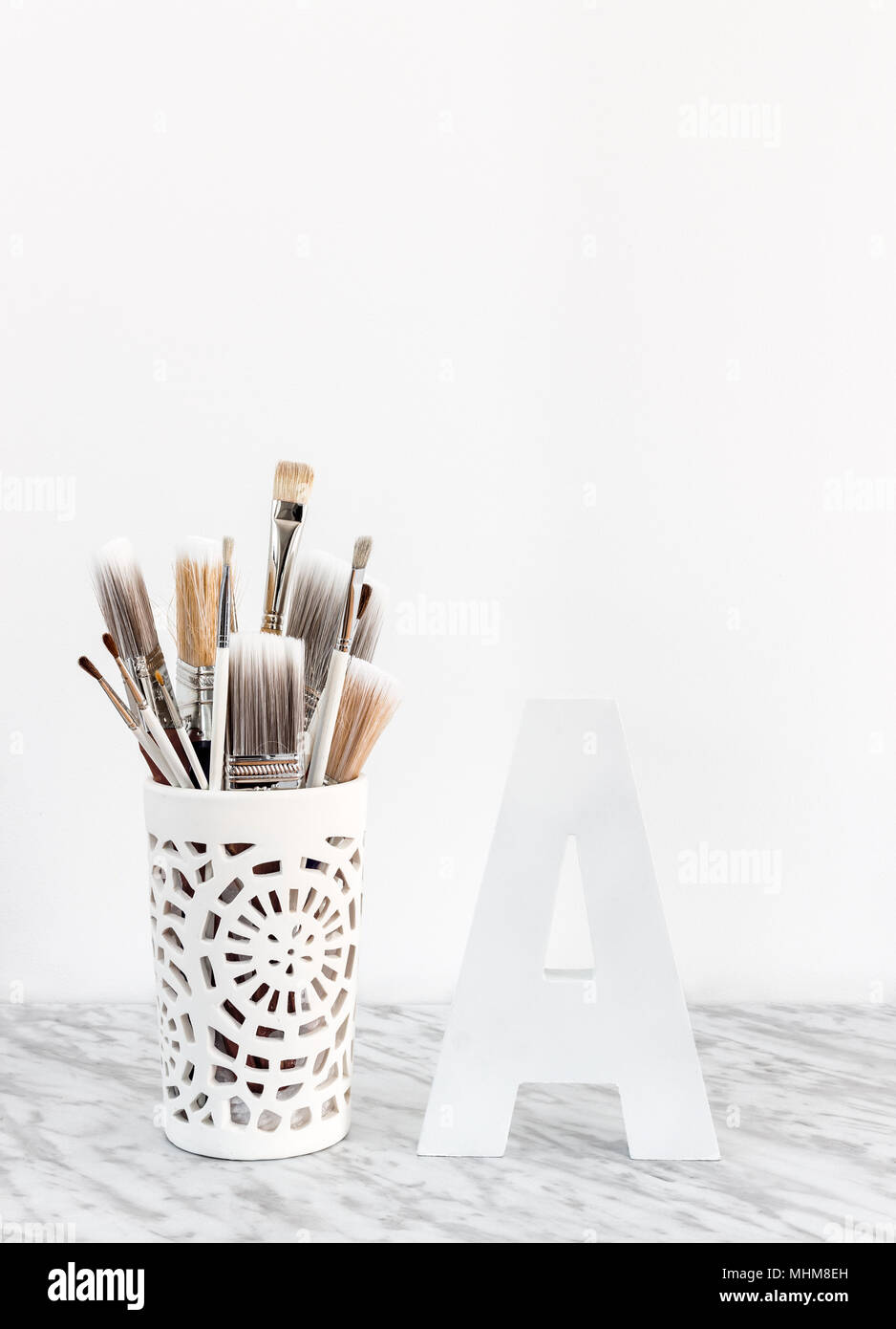 Paintbrushes in a decorative vase and white letter A on marble surface ...