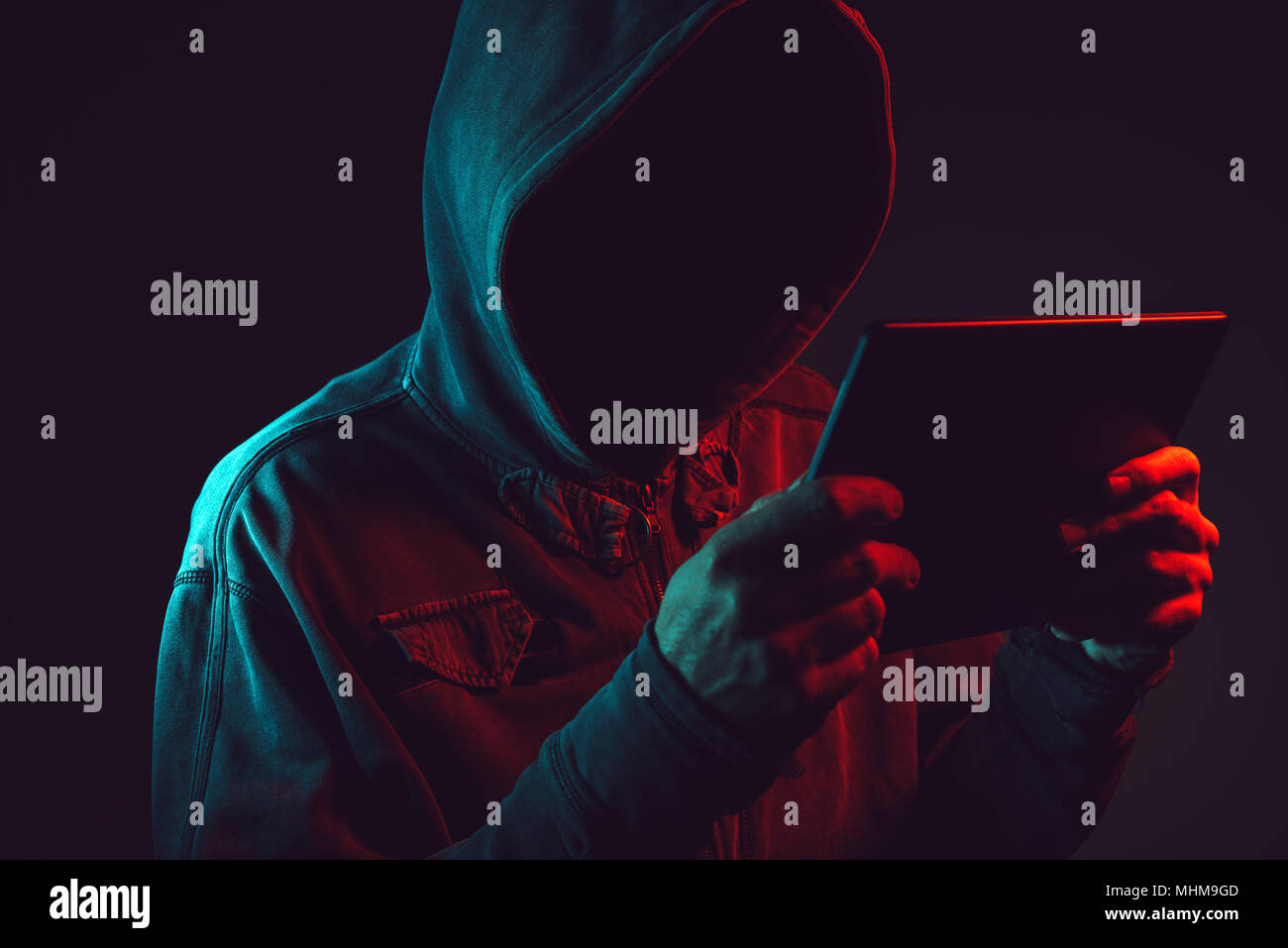 Hooded computer hacker with tablet computer, red and blue light low key ...