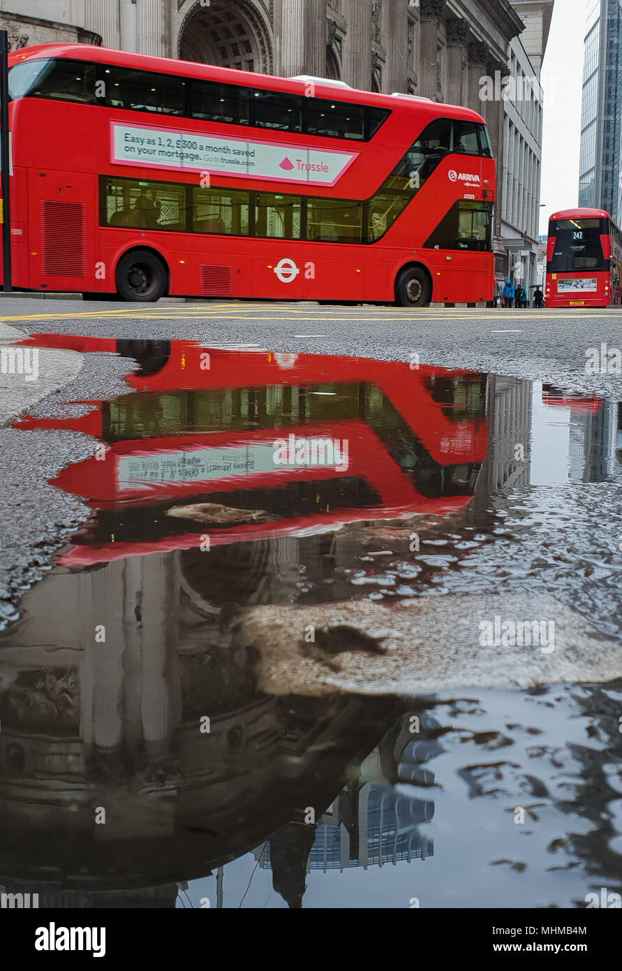 A red London bus reflected in a puddle of rain water. Featuring ...