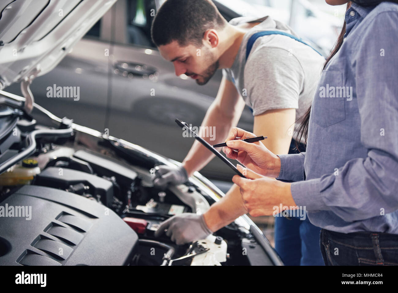A man mechanic and woman customer look at the car hood and discuss ...