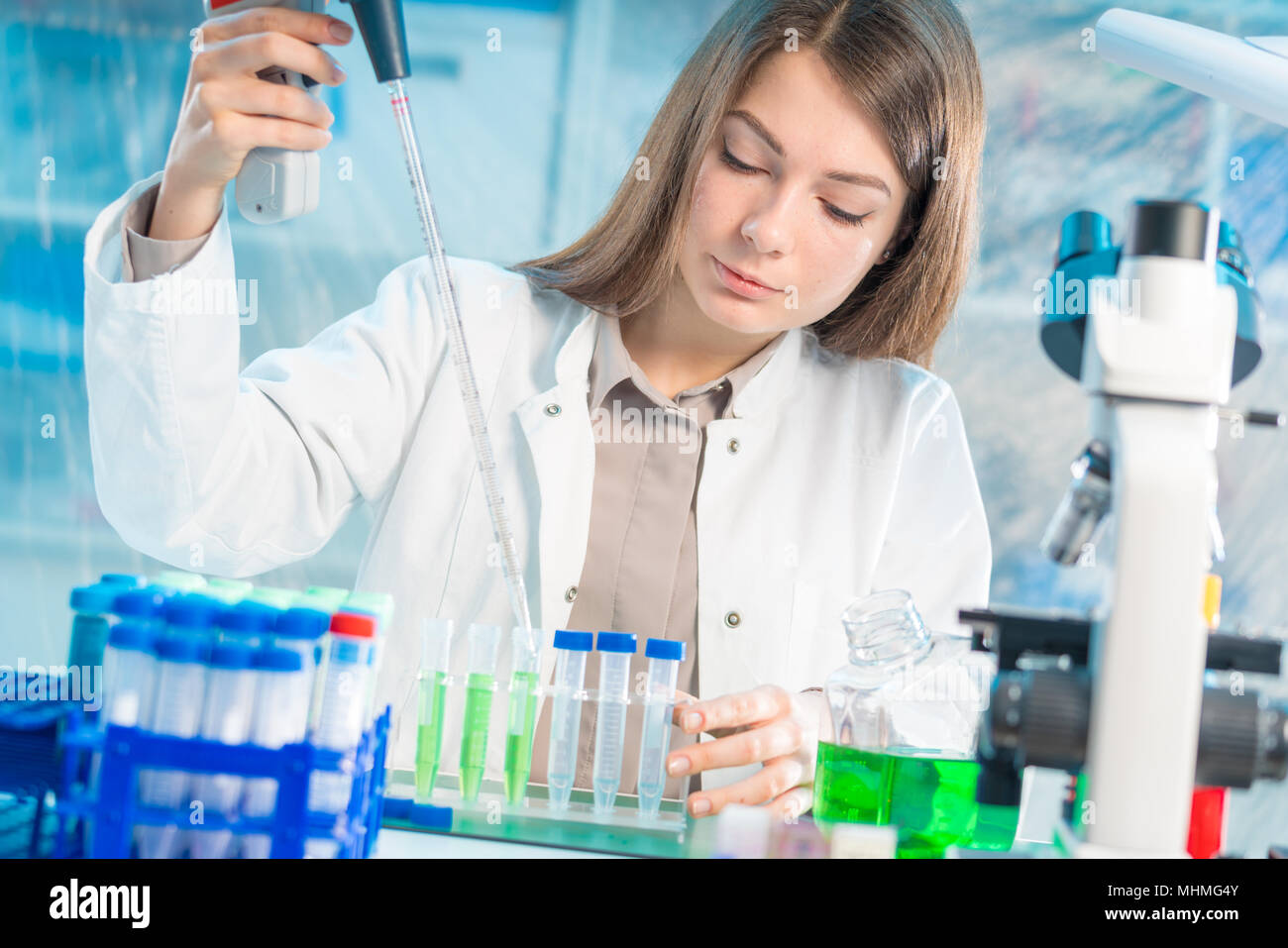 Young woman in scientific lab with pipette and chemicals in test tubes ...