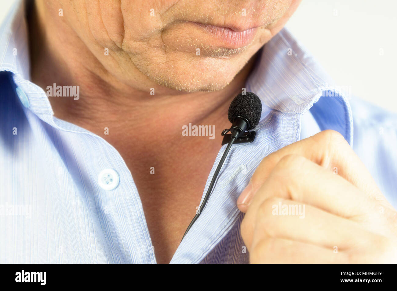 The lips of a man speak loudly in a whisper into a lapel microphone ...