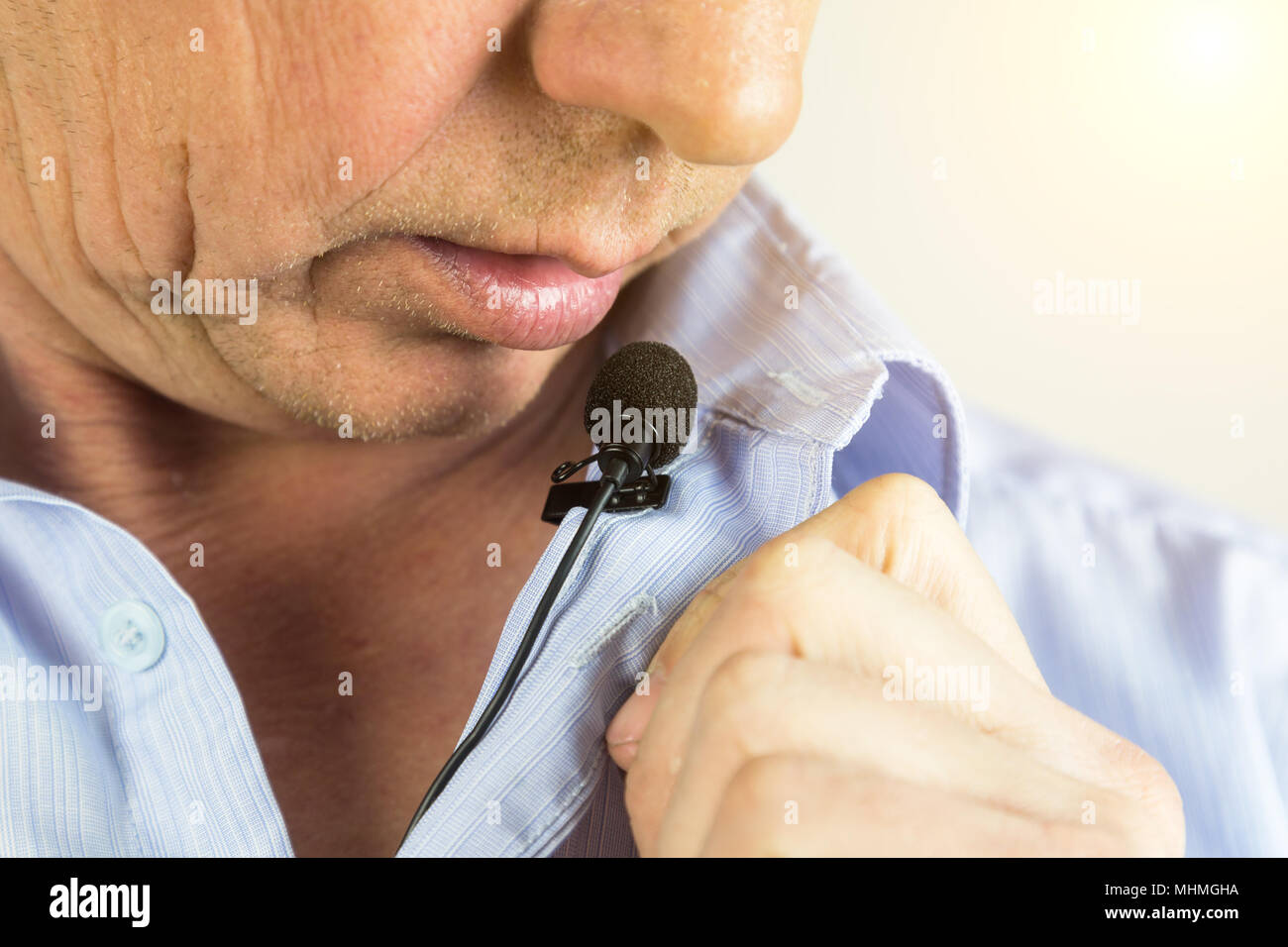 The lips of a man speak loudly in a whisper into a lapel microphone ...